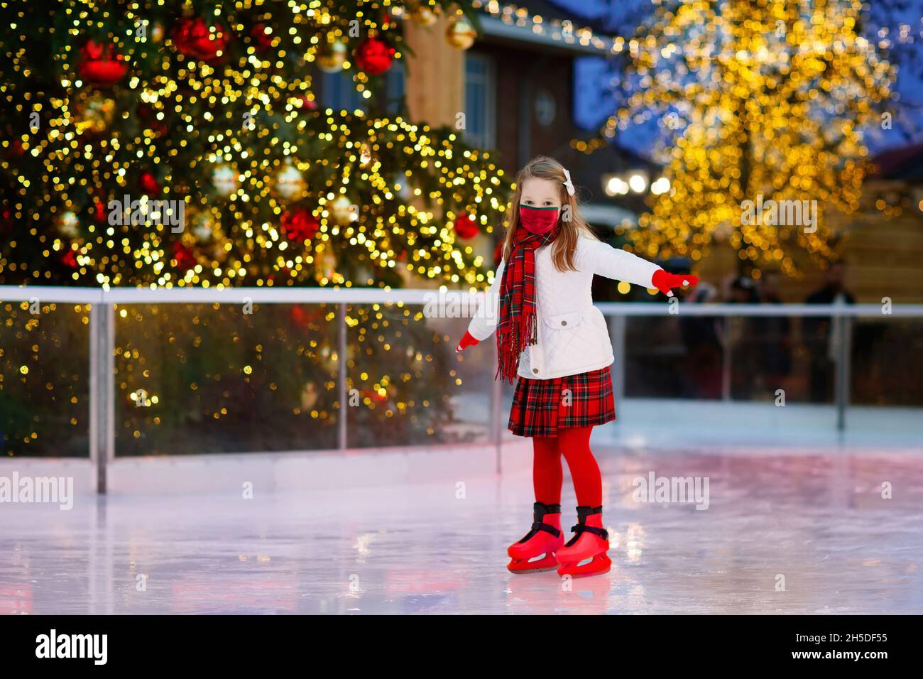 Kid in face mask ice skating in winter park rink. Safe Christmas fun in ...
