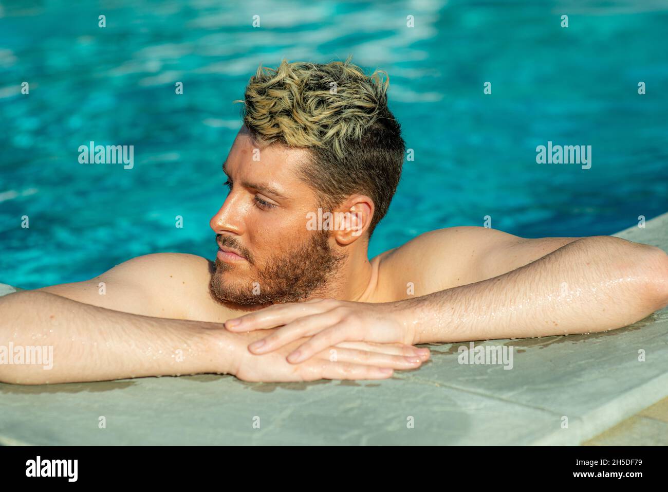 young man leaning in a swimming pool edge with his hand and enjoying ...