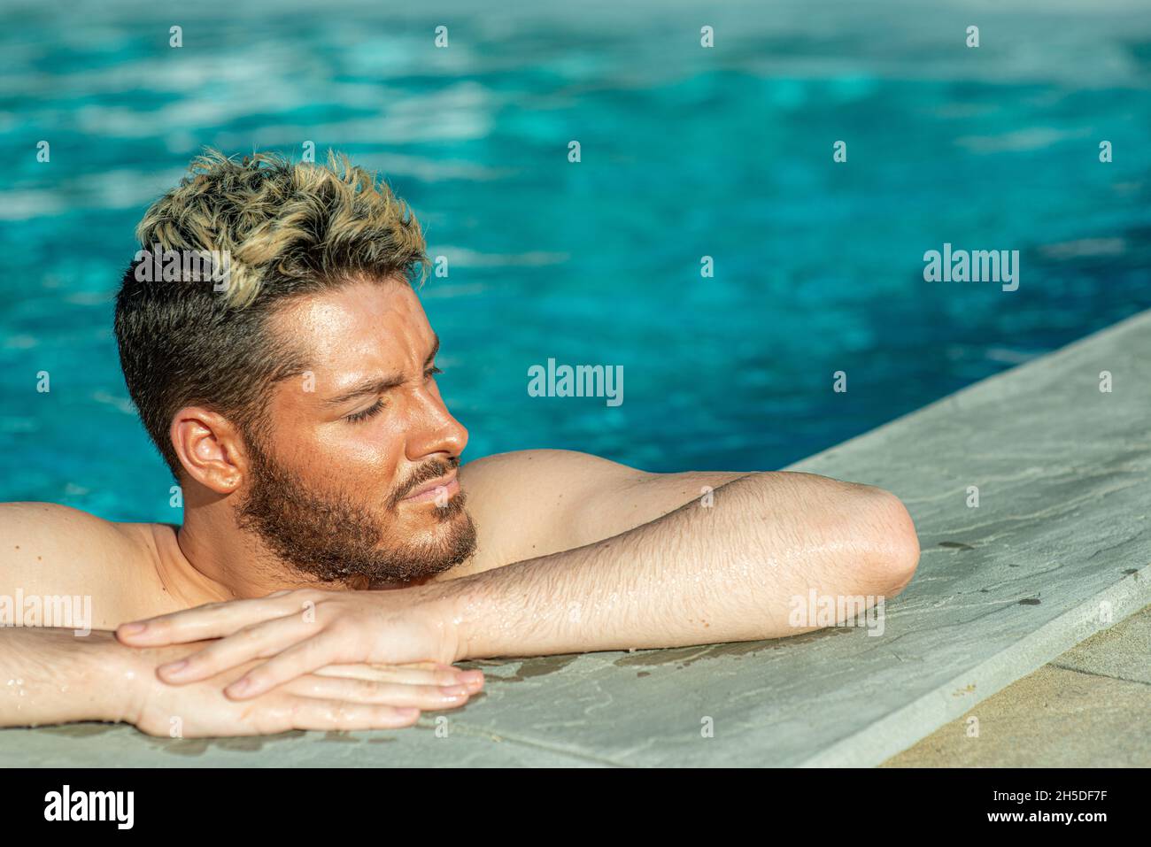 young man leaning in a swimming pool edge with his hand enjoying the ...