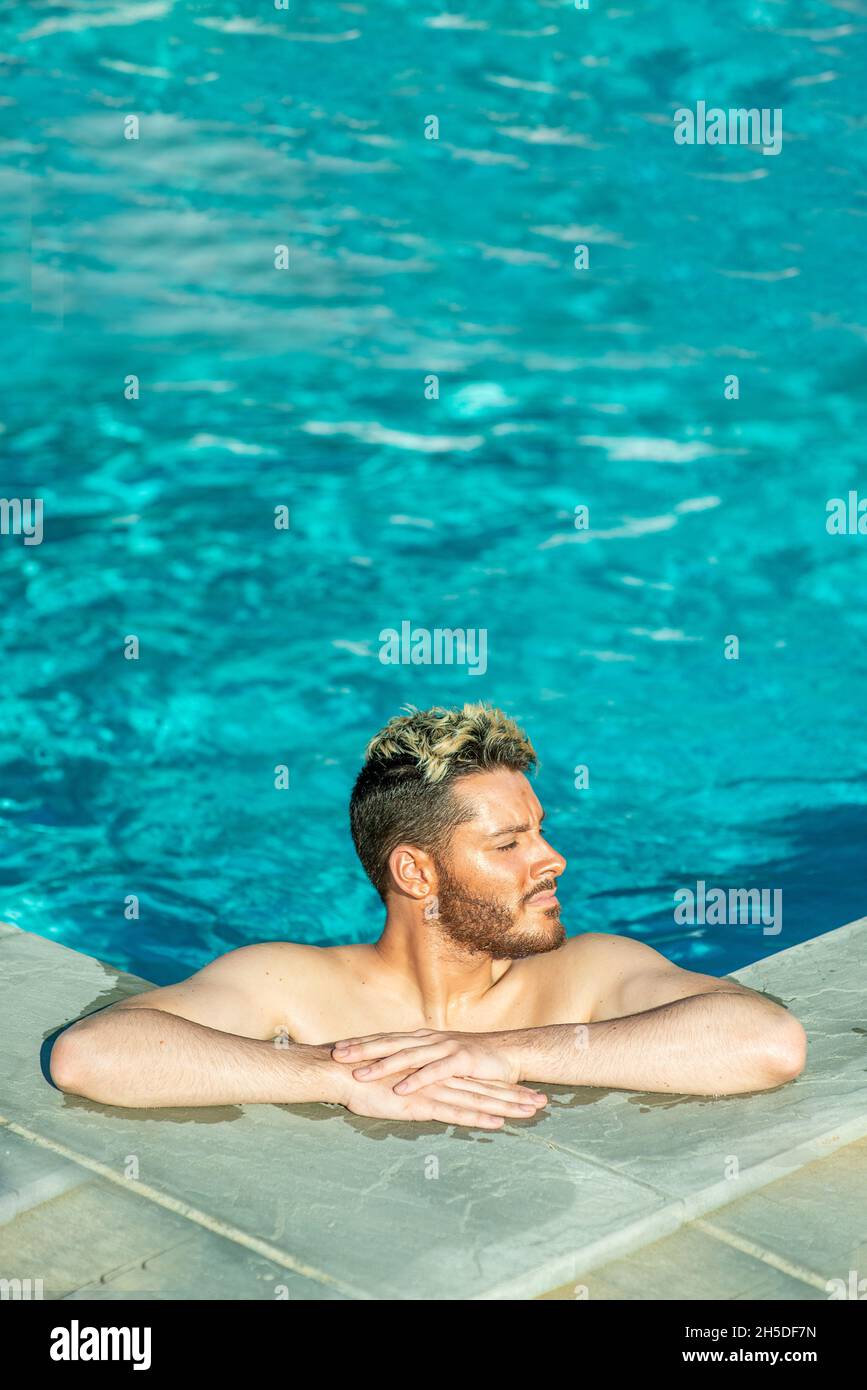 Vertical high angle shot of a young man leaning in a swimming pool edge ...