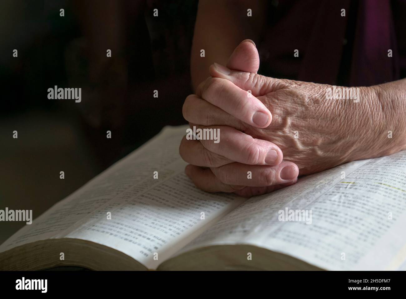 Close Up View Of Senior Woman Hands On Open Bible Folded In Prayer