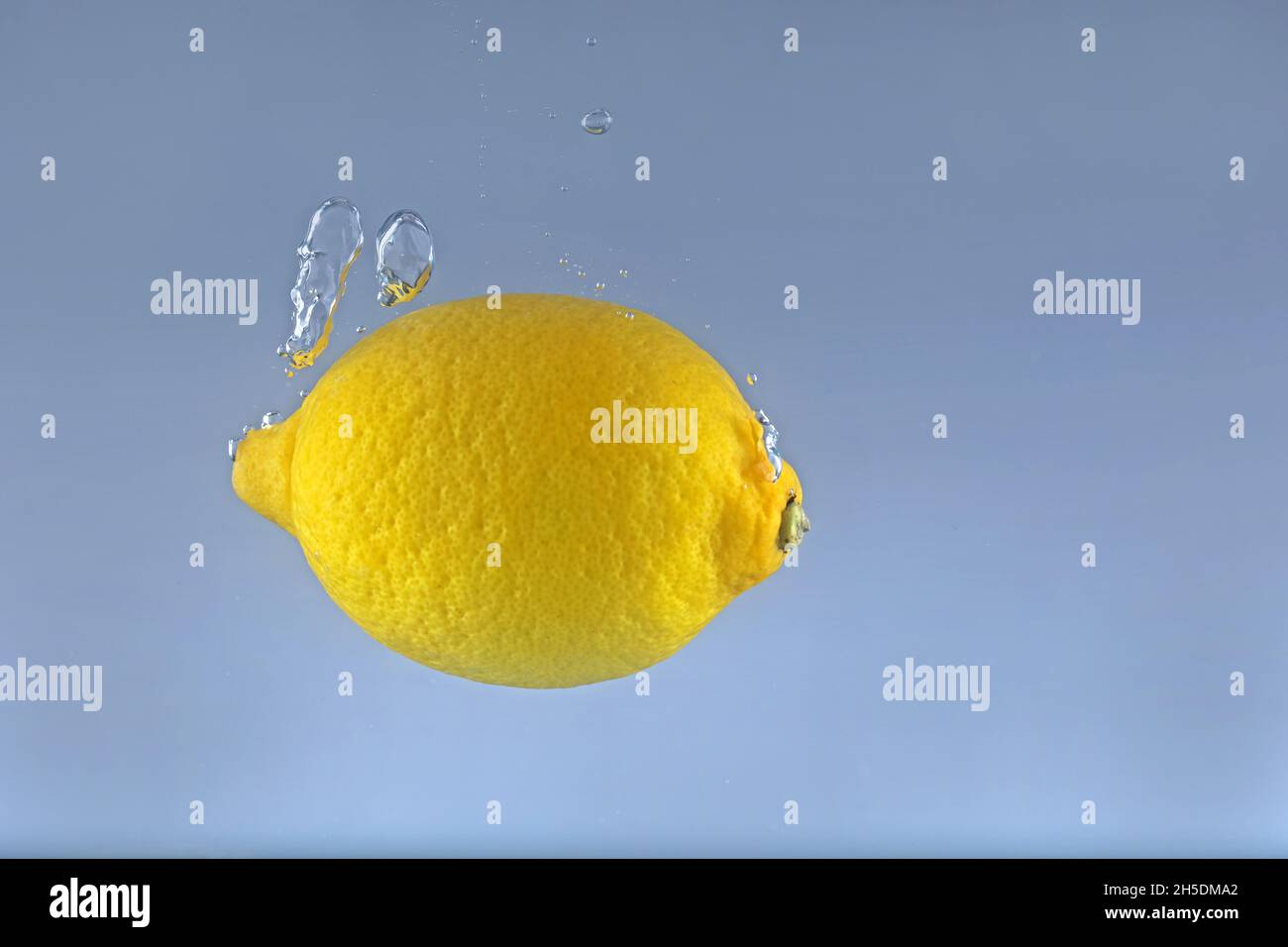 Whole lemon falls into the water with a splash and air bubbles on a ...