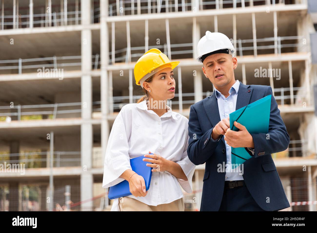 Two young successful architects on the construction site, discuss the ...