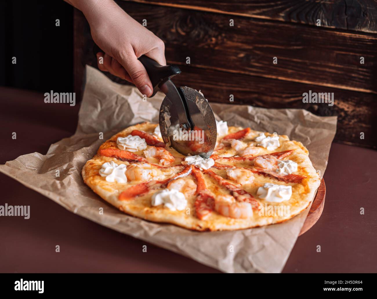Cutting fish and shrimp pizza into equal pieces with special knife ...