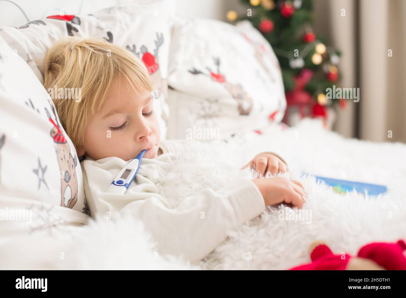 Beautiful blond toddler child, sick boy with fever, lying in bed on ...