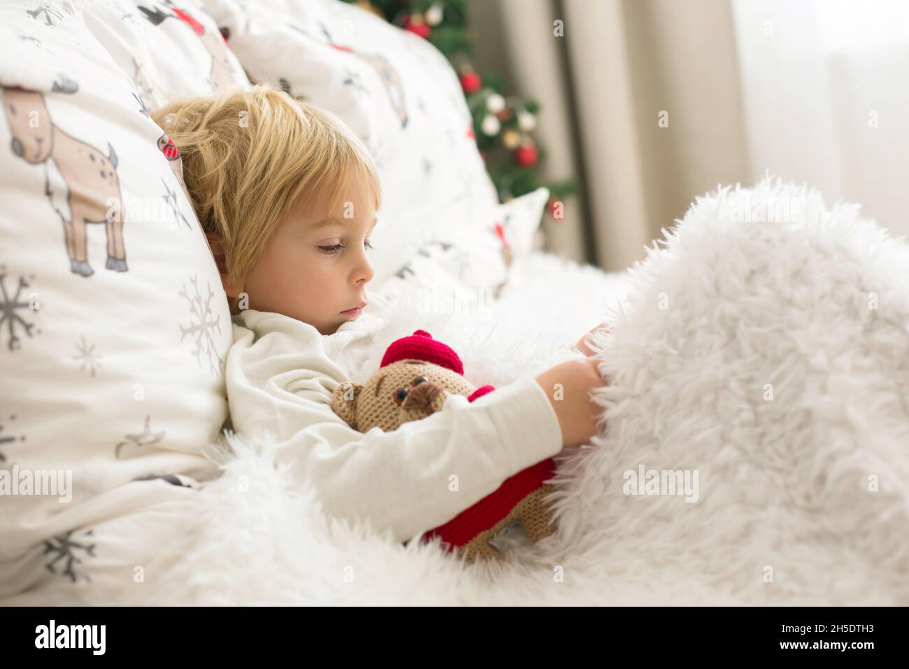 Beautiful blond toddler child, sick boy with fever, lying in bed on ...