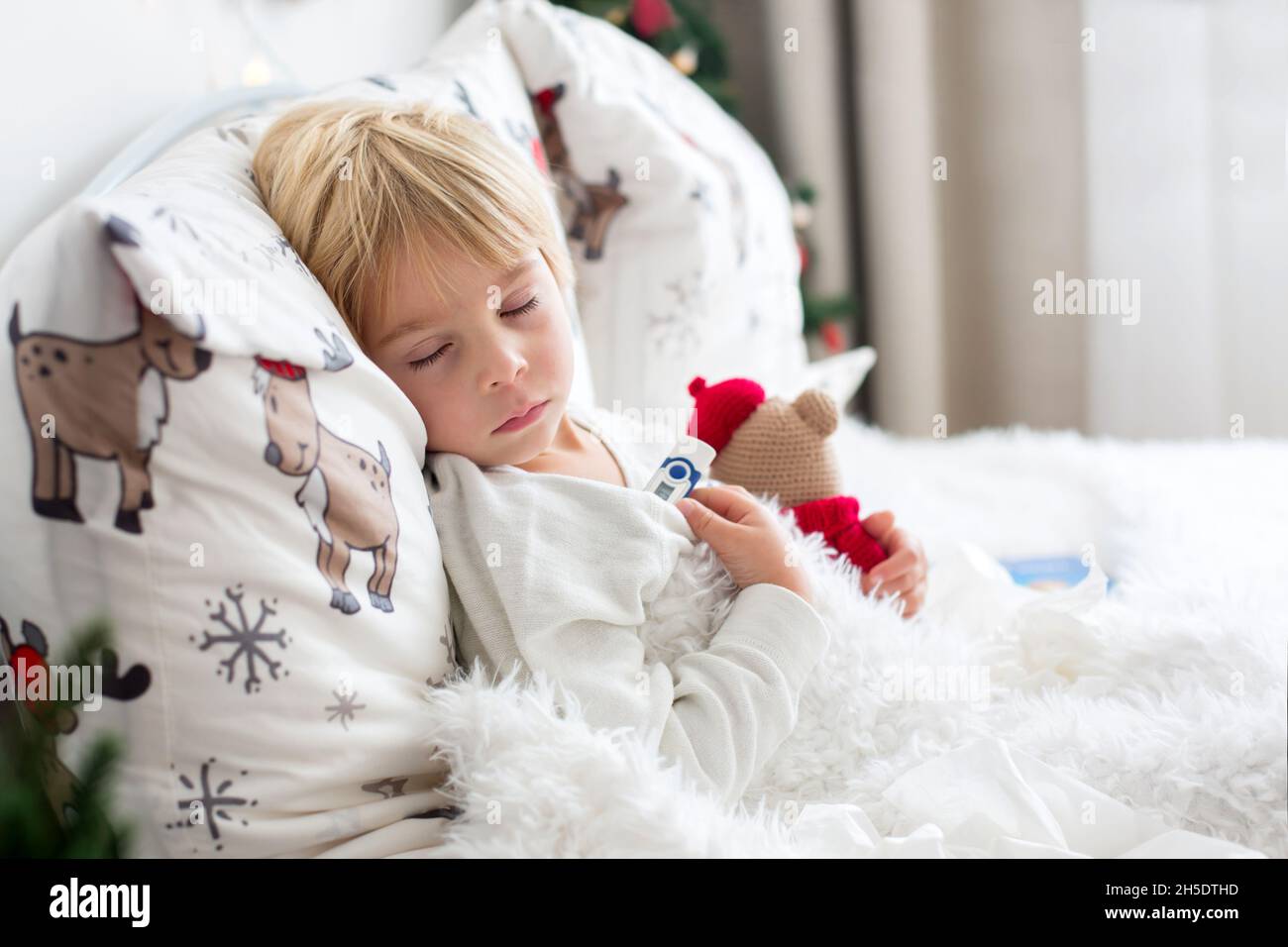 Beautiful blond toddler child, sick boy with fever, lying in bed on ...