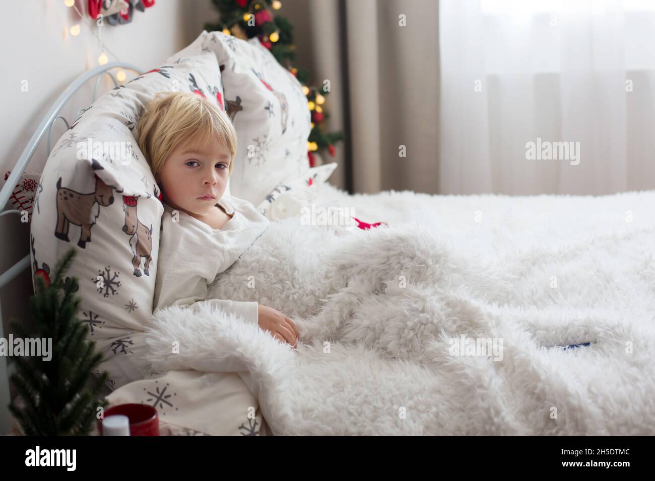 Beautiful blond toddler child, sick boy with fever, lying in bed on ...