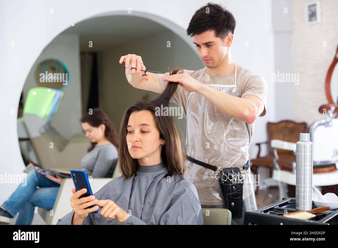 Girl client using phone during hair cut by professional hairdresser ...
