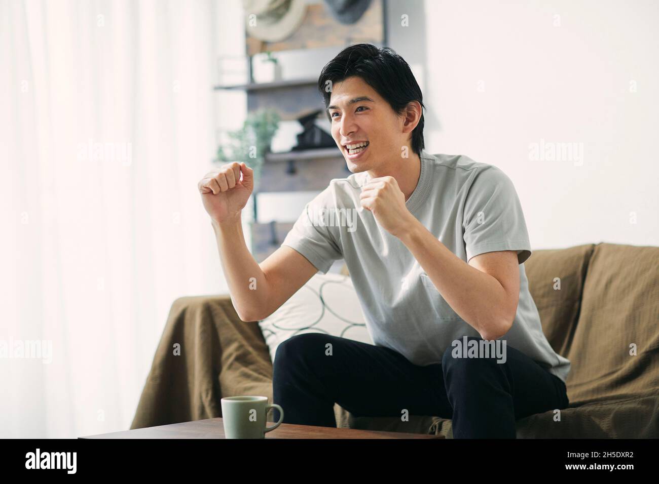 Japanese man cheering on the sofa Stock Photo - Alamy