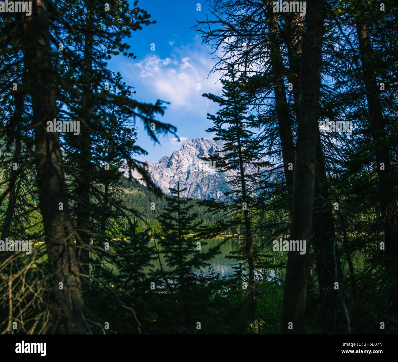 Beautiful view of a lake seen through the forest trees and a mountain ...