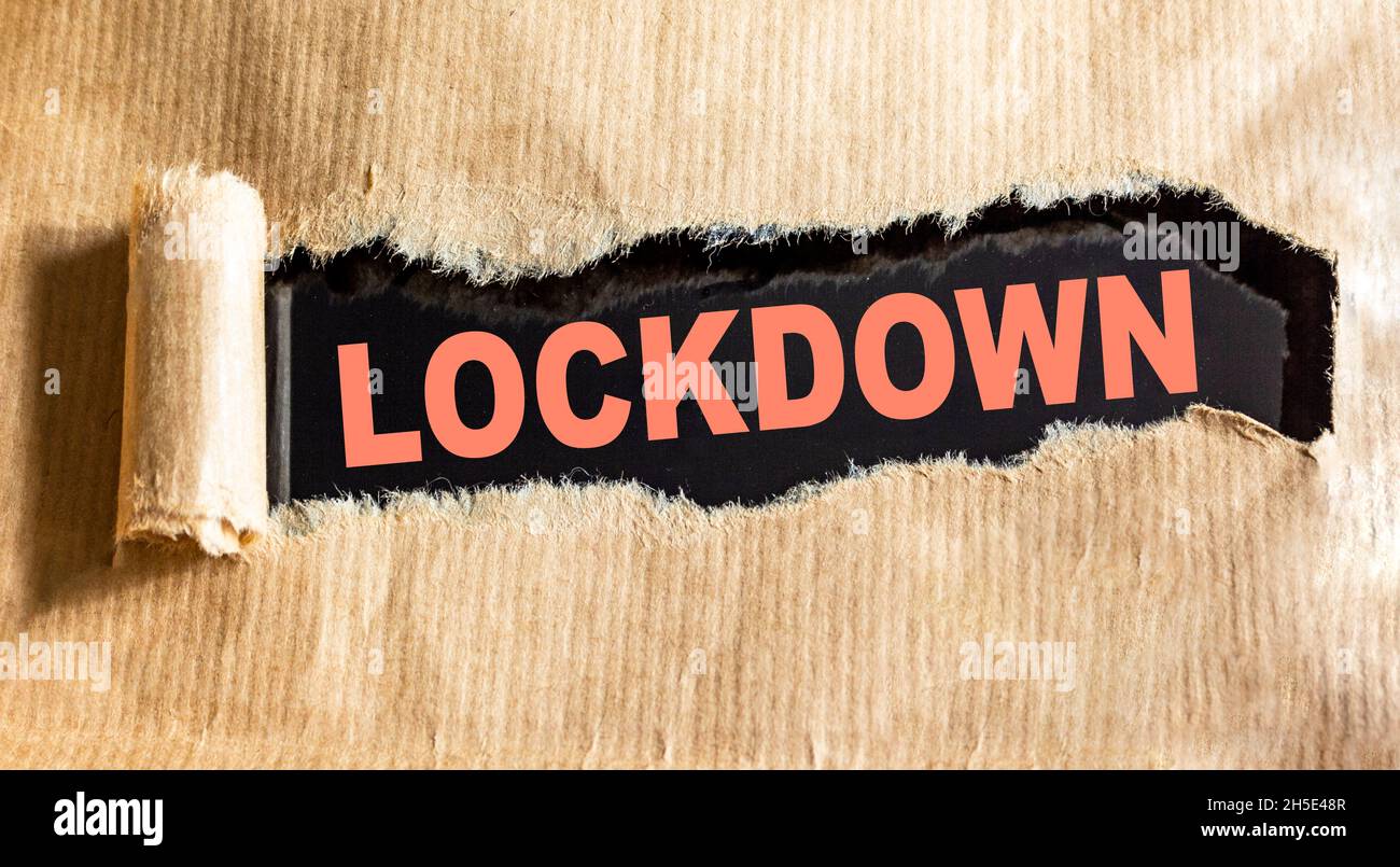 LOCKDOWN word seen through torn paper on black background. Second wave ...
