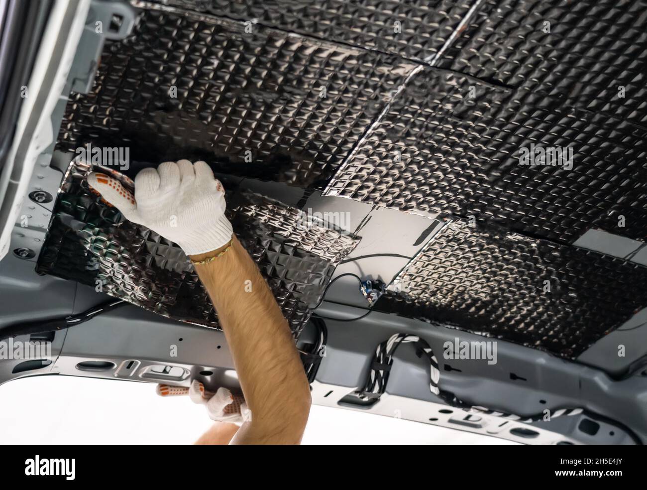 Worker hands glues soundproofing material to inside of car roof ...