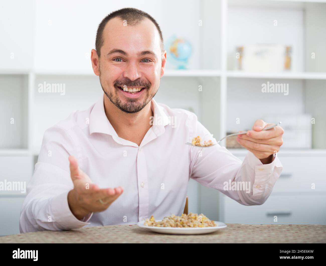 Positive young man eating porridge Stock Photo - Alamy