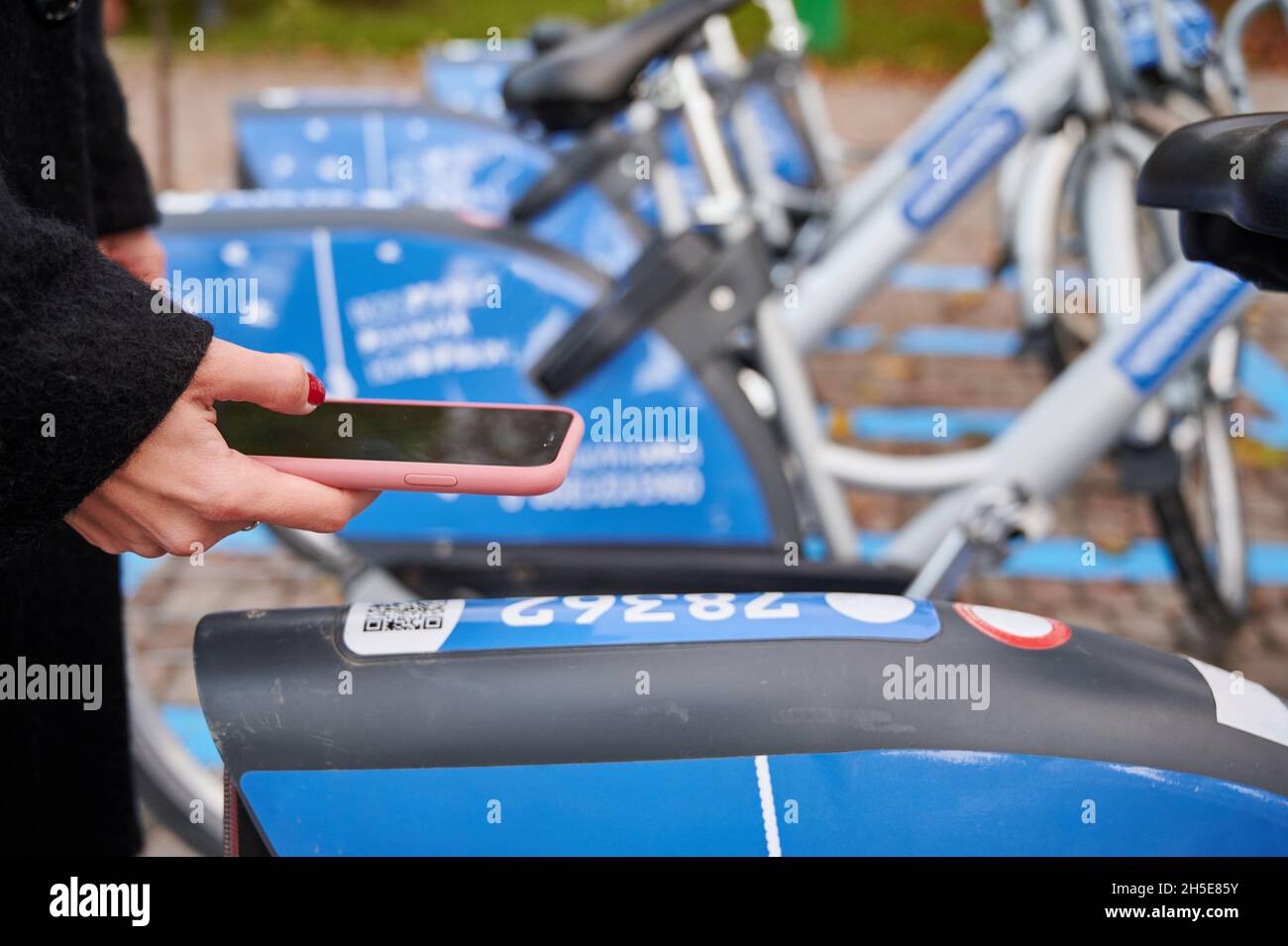 Side view of woman's hand with smartphone scaning QR code to rent a ...