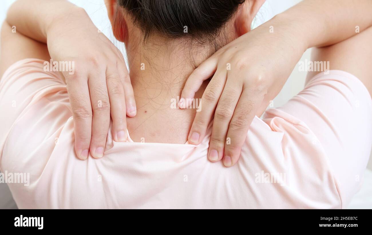 Back view of Asian woman using hands to massage the nape of her neck in ...
