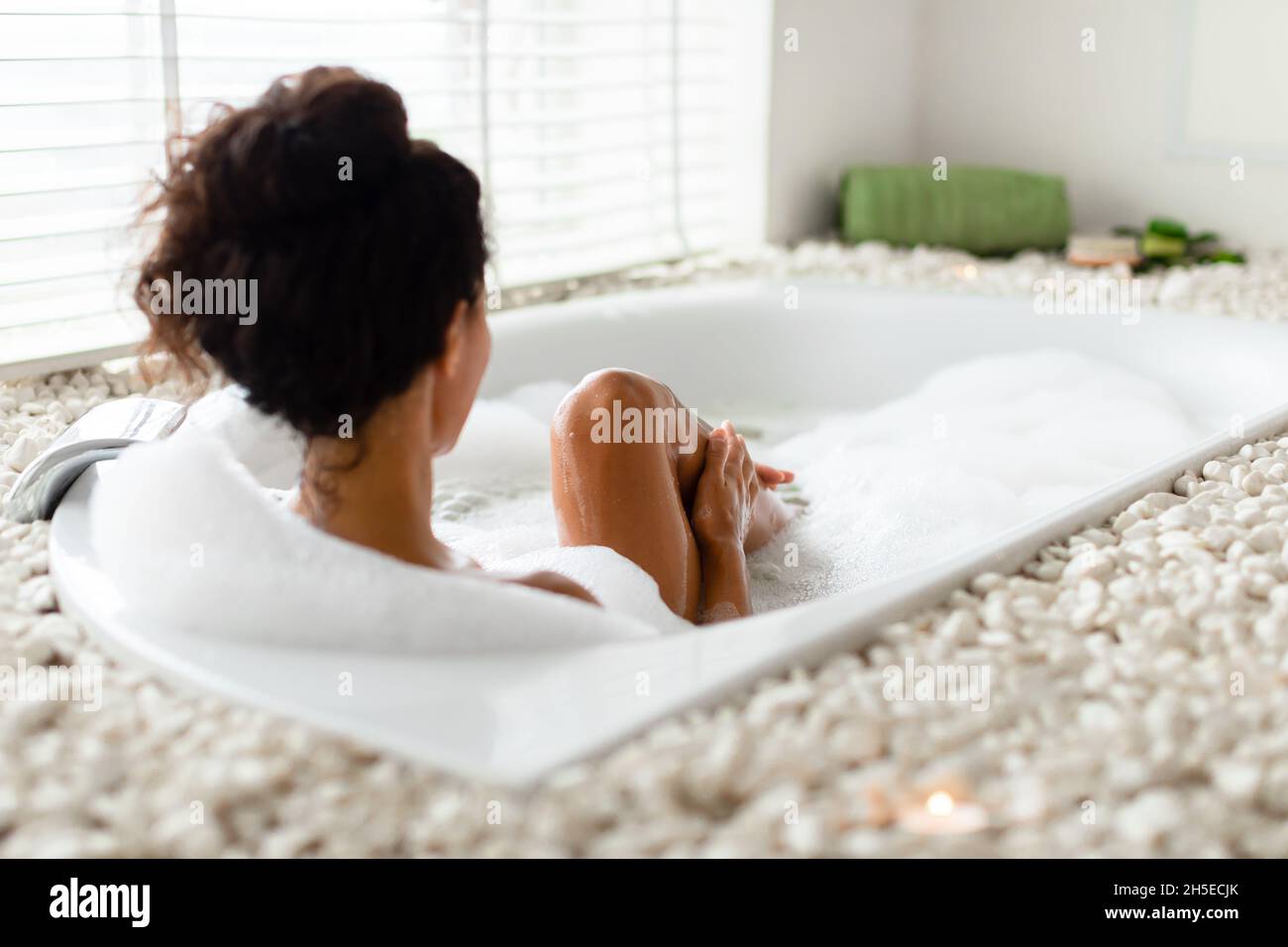 Back view of young woman relaxing in bath with foam, touching her silky ...