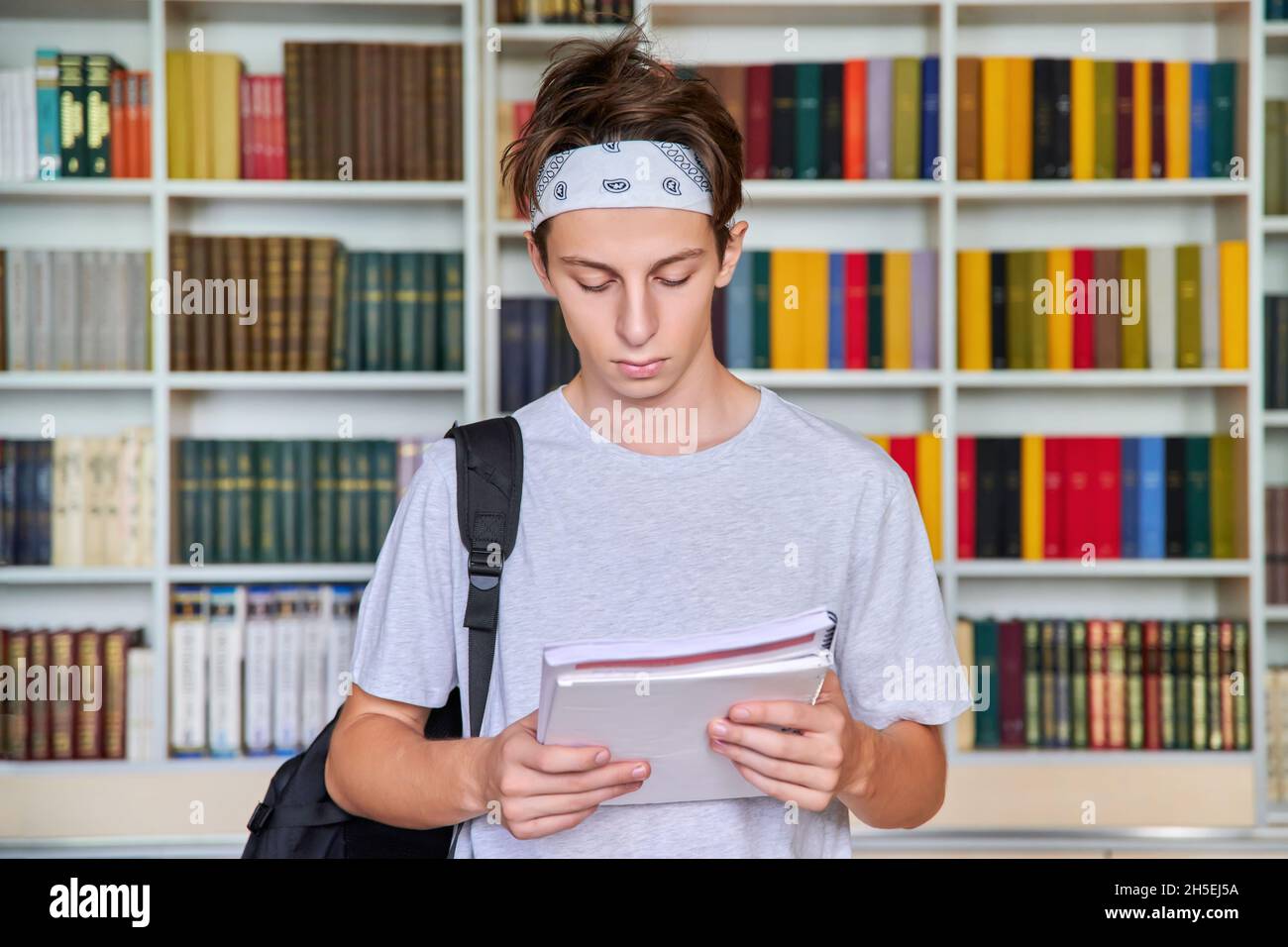 Portrait of a male teenager student looking in a notebook in a library ...