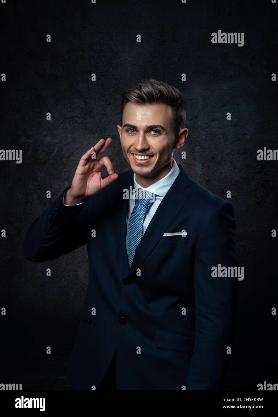 A young male steward, in a suit, smiles, makes a hand gesture ...