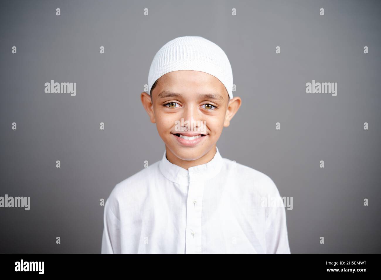 smiling Muslim child with traditional cap by looking at camera on gray ...