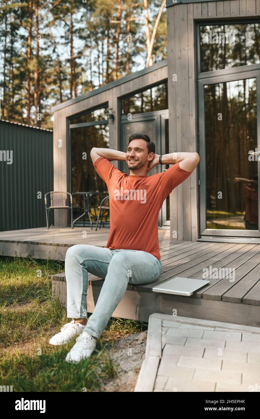 Smiling stretching man sitting on porch of house Stock Photo - Alamy