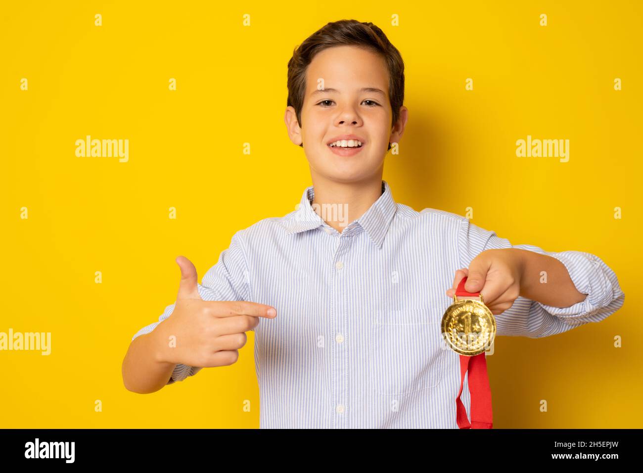 Cute child boy showing his gold medal isolated over yellow background ...