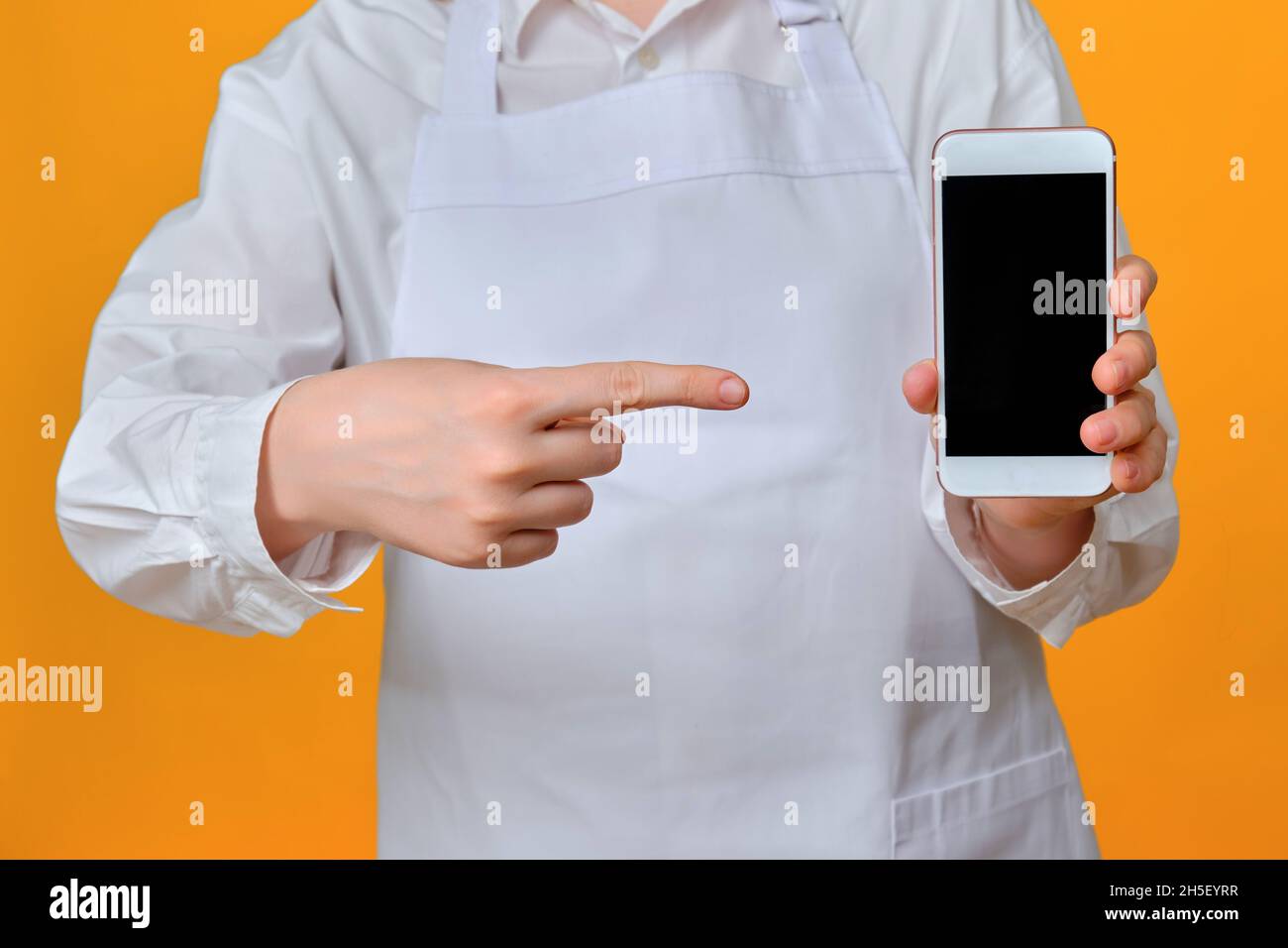 Man chef showing phone screen on yellow studio background, mockup copy ...