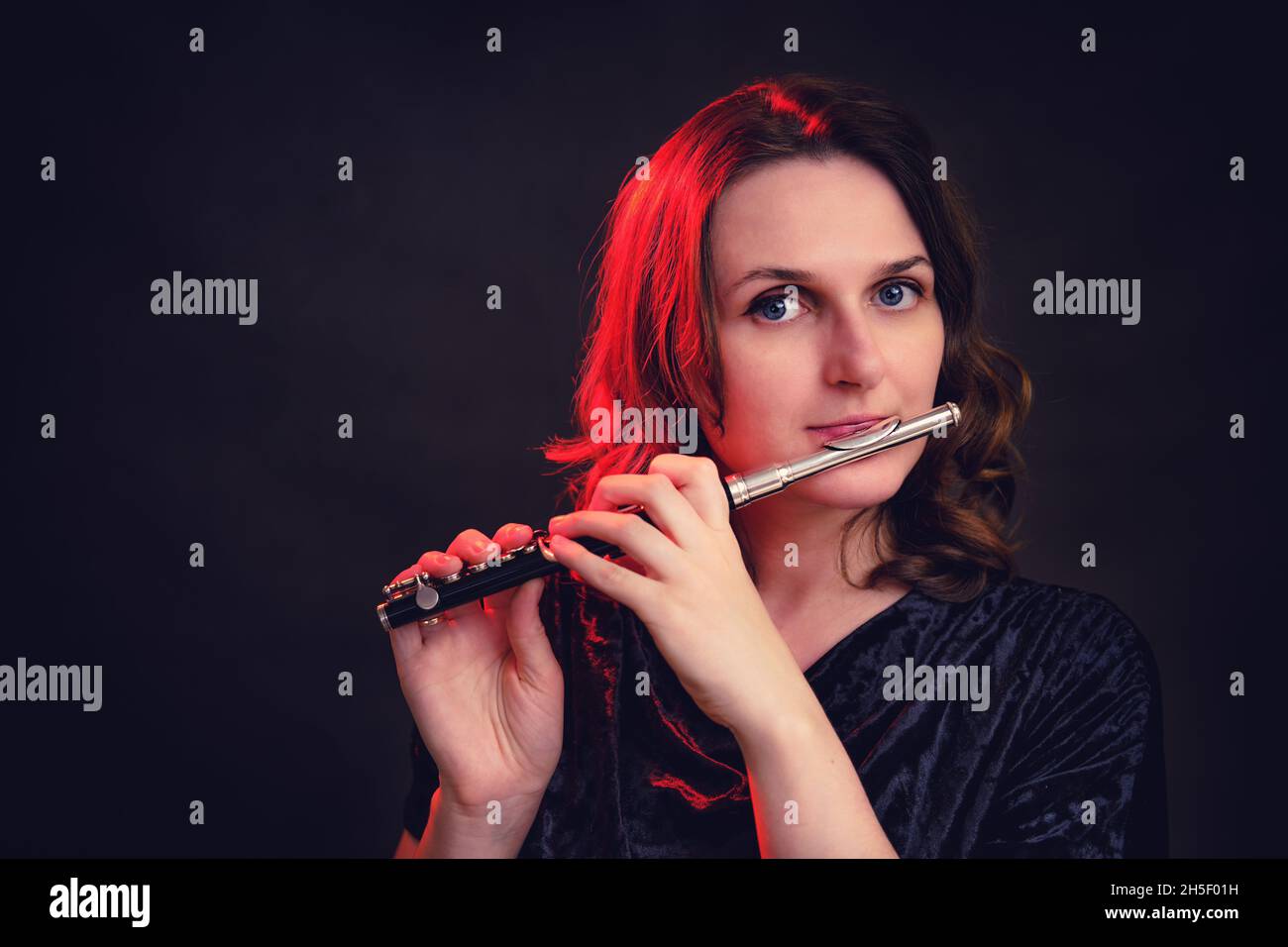 Portrait of a woman musician with a piccolo flute on a studio black ...