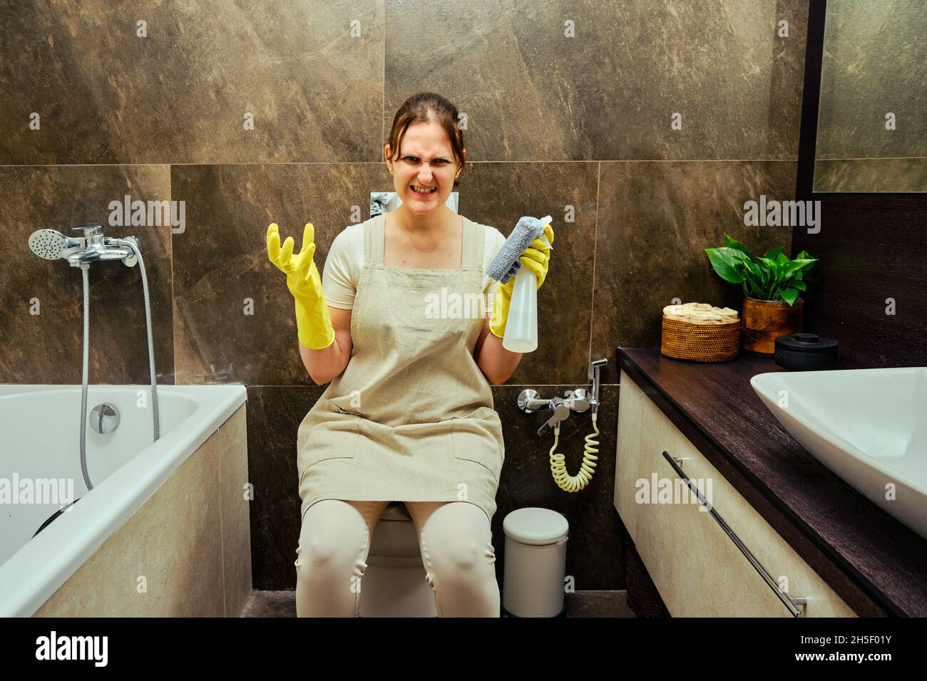 Angry woman sits on the toilet while cleaning the bathroom ...