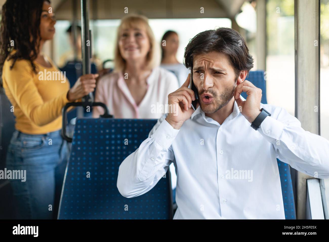 Confused guy talking on phone holding finger in ear Stock Photo - Alamy