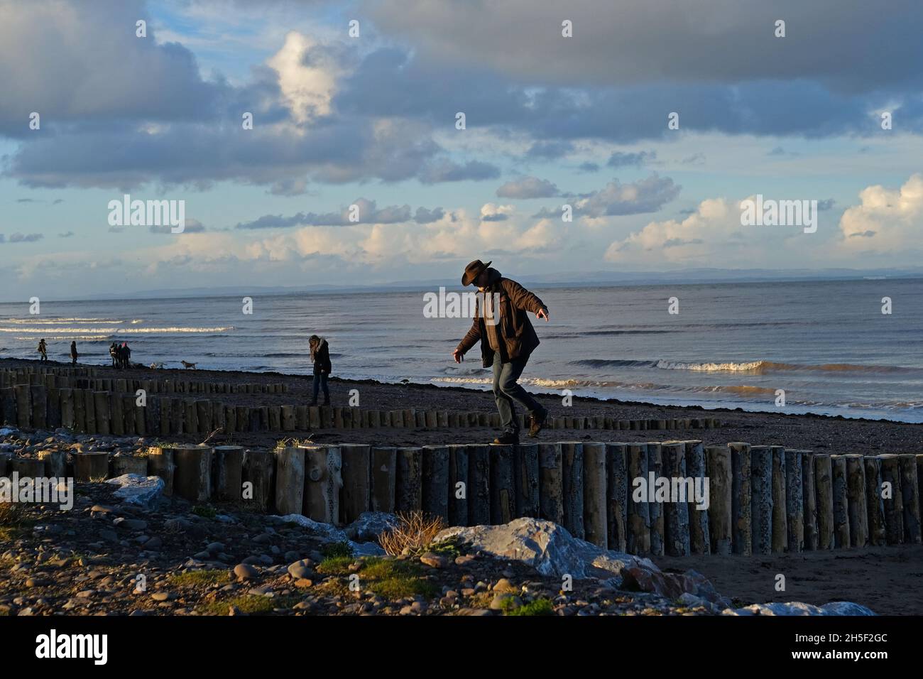 A older man balancing, walking on a wooden groyne on Dunster beach ...