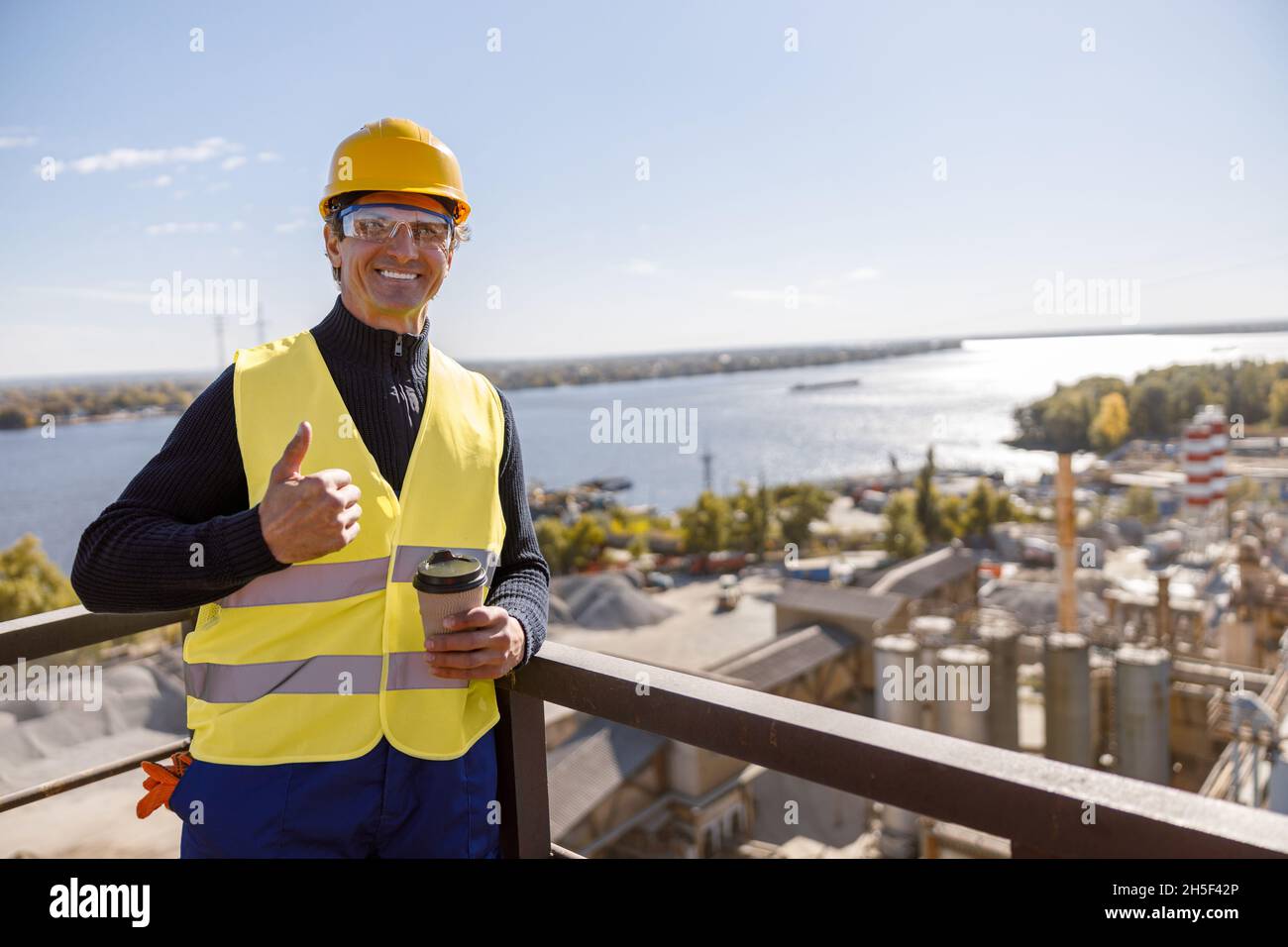 Cheerful male engineer holding cup of coffee and giving thumbs up Stock ...