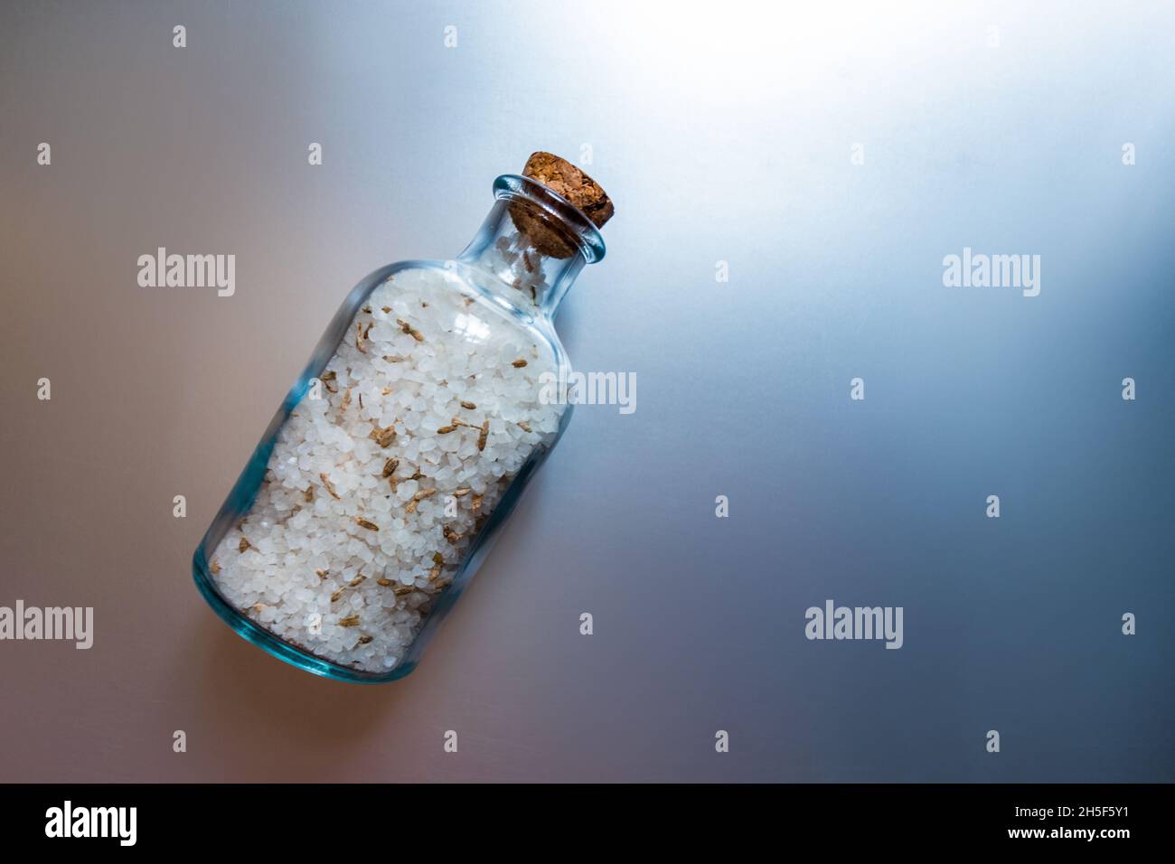 A transparent glass container with sea white salt lies on a metal ...