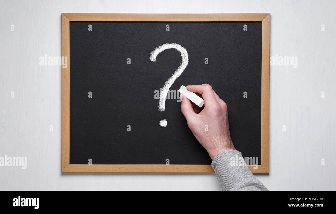 Male hand draws a question mark on the blackboard with chalk. The ...