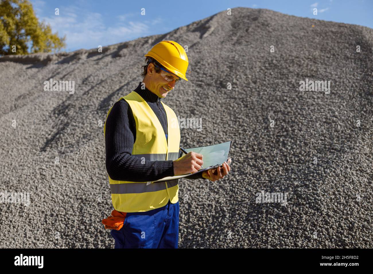 Cheerful man writing documents outdoors at cement factory Stock Photo ...