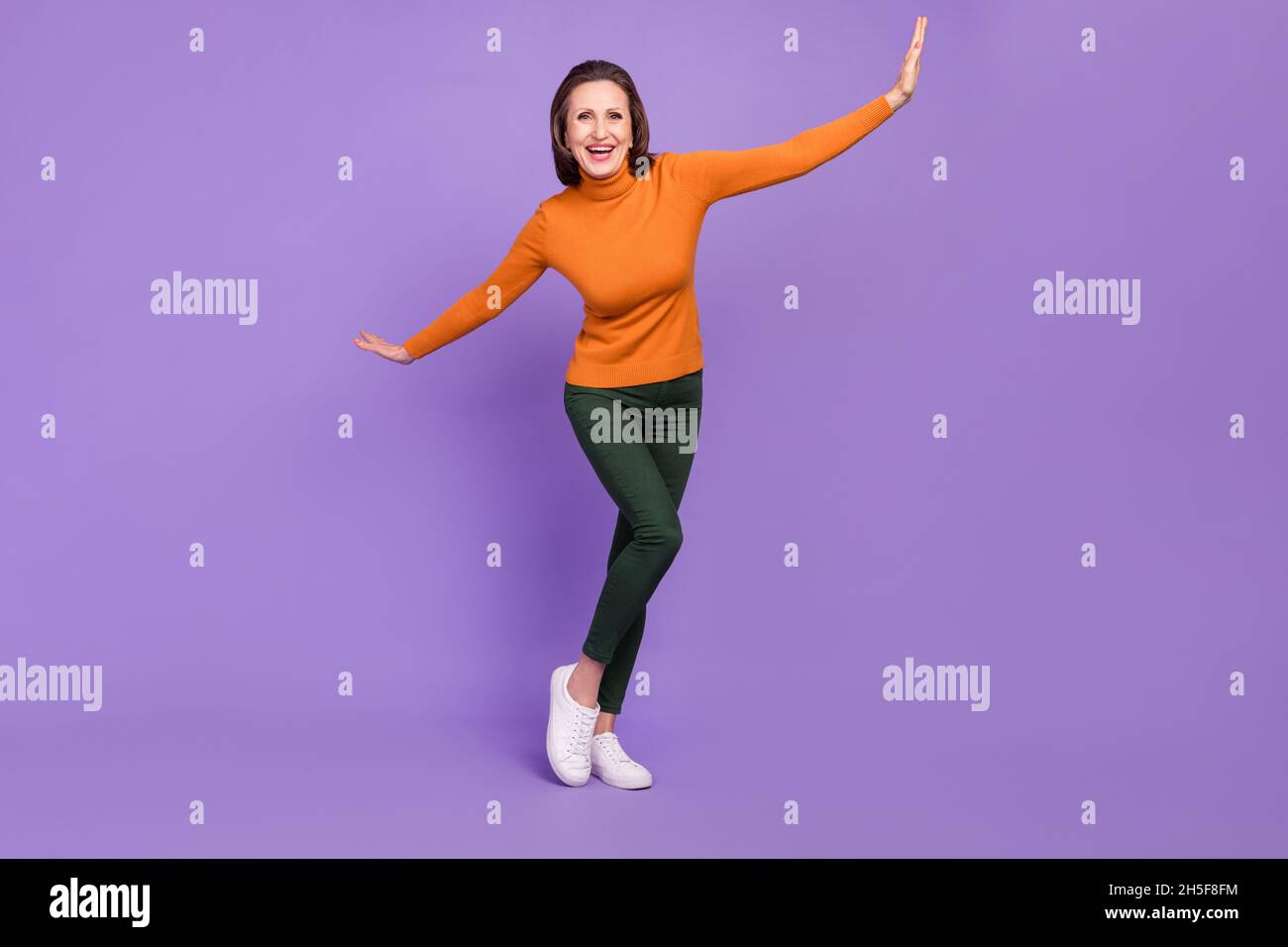 Photo of charming childish retired woman wear orange pullover dancing arms sides smiling ...