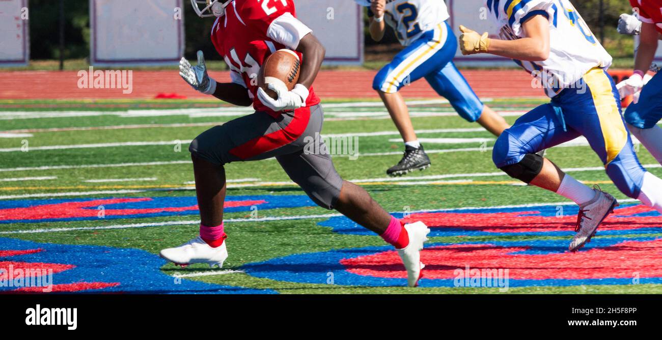 A high school football player is running with the ball being chased by ...
