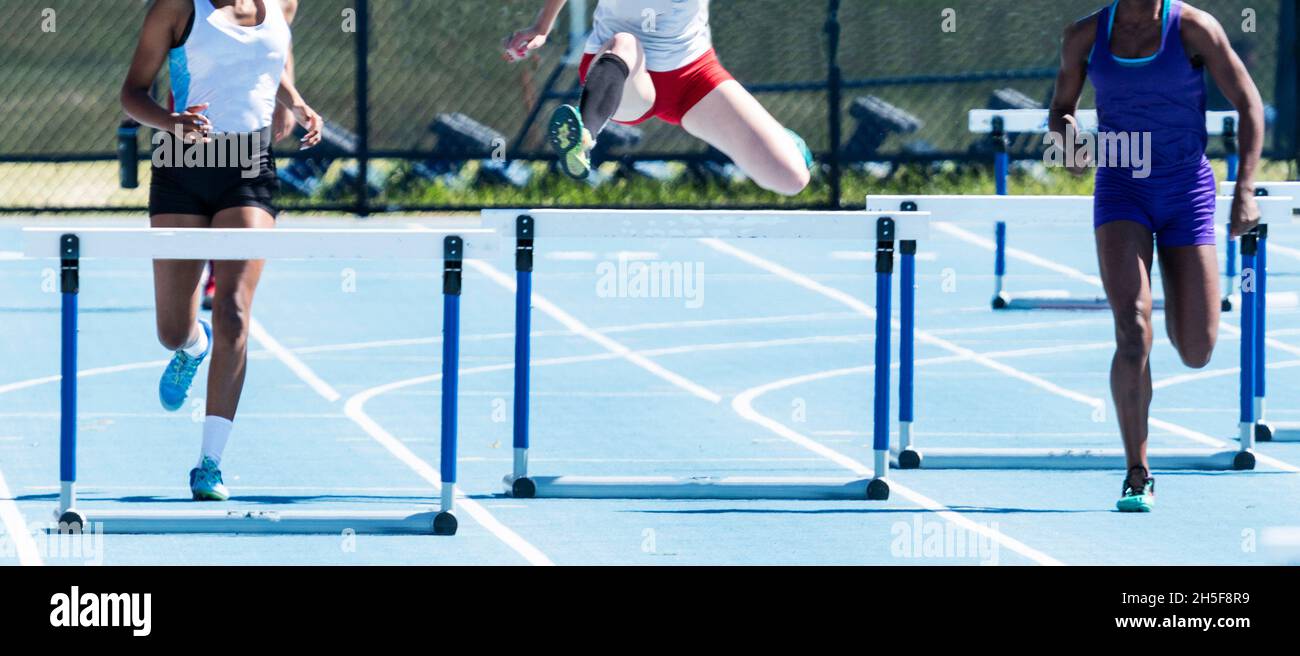 Front view of three high school girls running in a 400 meter hurlde ...