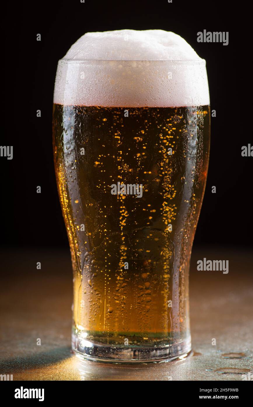 Vertical shot of a glass of cold refreshing beer with foam on a wooden ...
