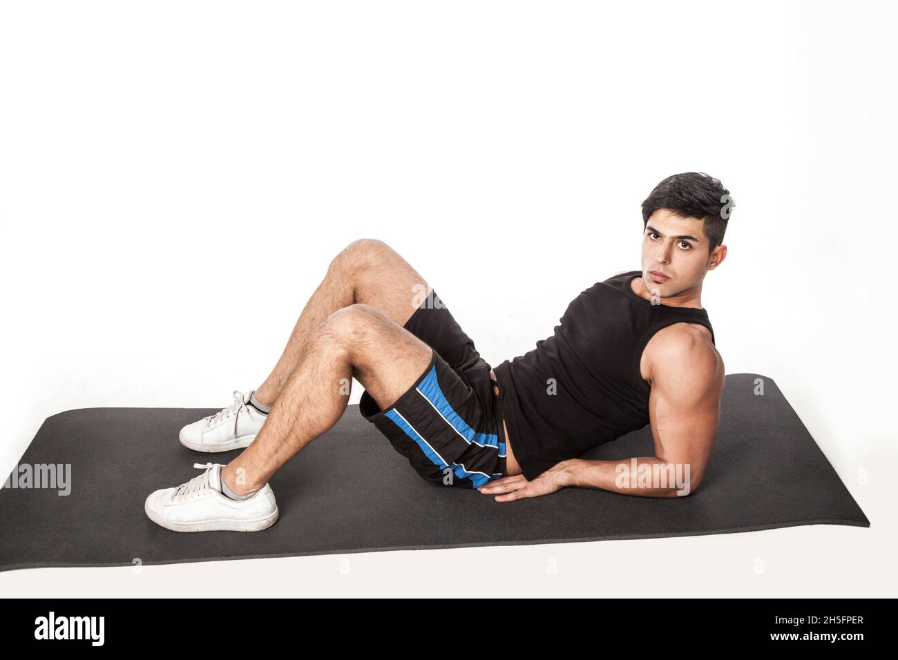 Portrait of handsome confident man lying on fitness mat, looking at ...