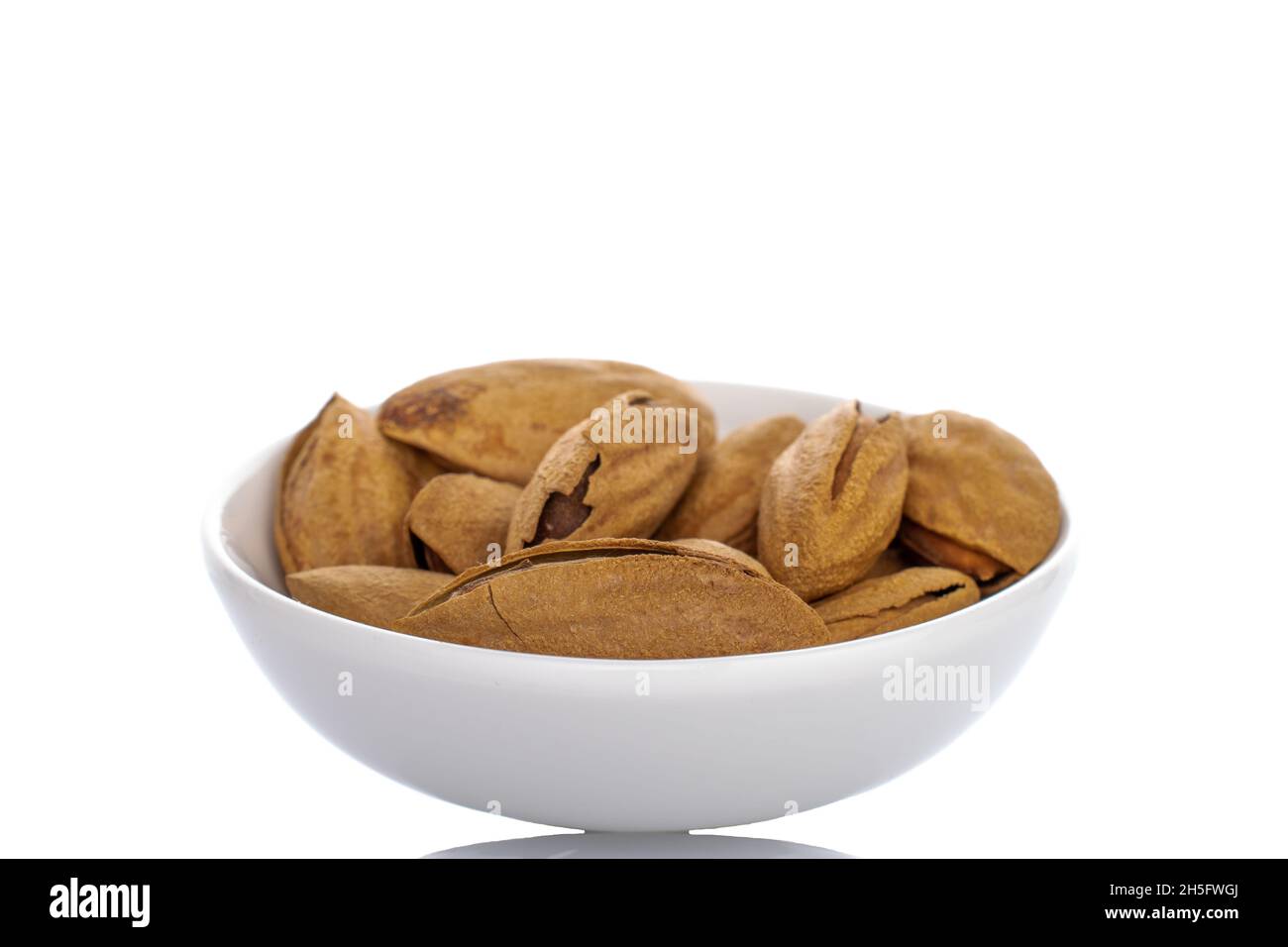Dried unpeeled almonds in a white ceramic saucer, close-up, isolated on ...