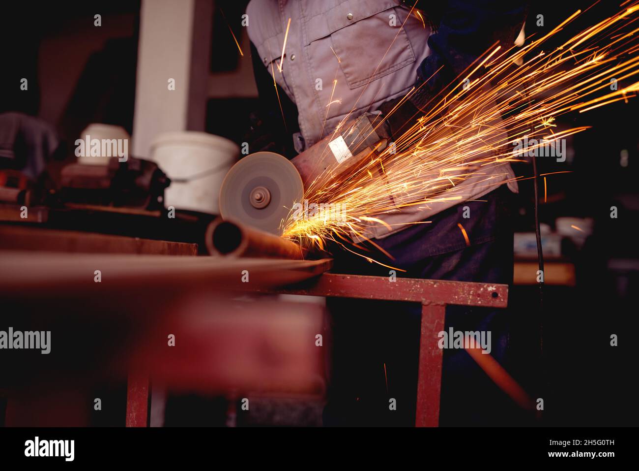 Craftsman sawing metal sparkles all around workshop. Working late night ...