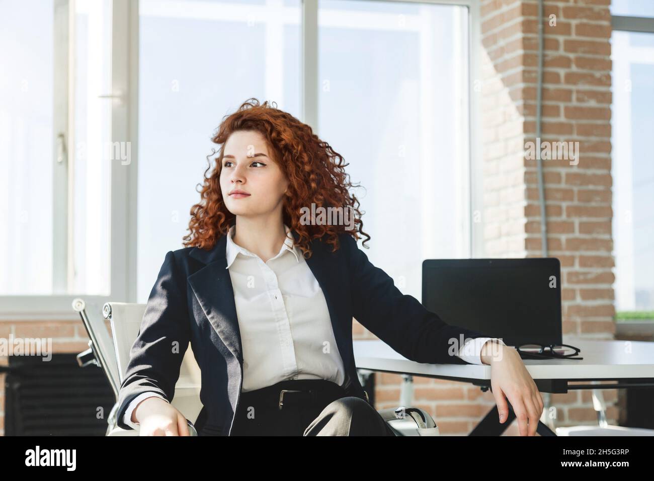 Portrait of a beautiful successful young business woman with red curly hair in the office ...