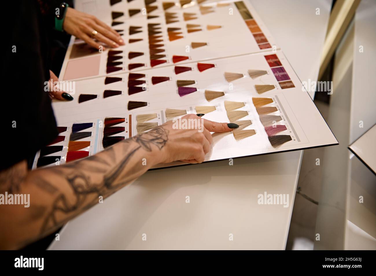 Close-up of a well-groomed tattooed hairdresser arm pointing to a ...