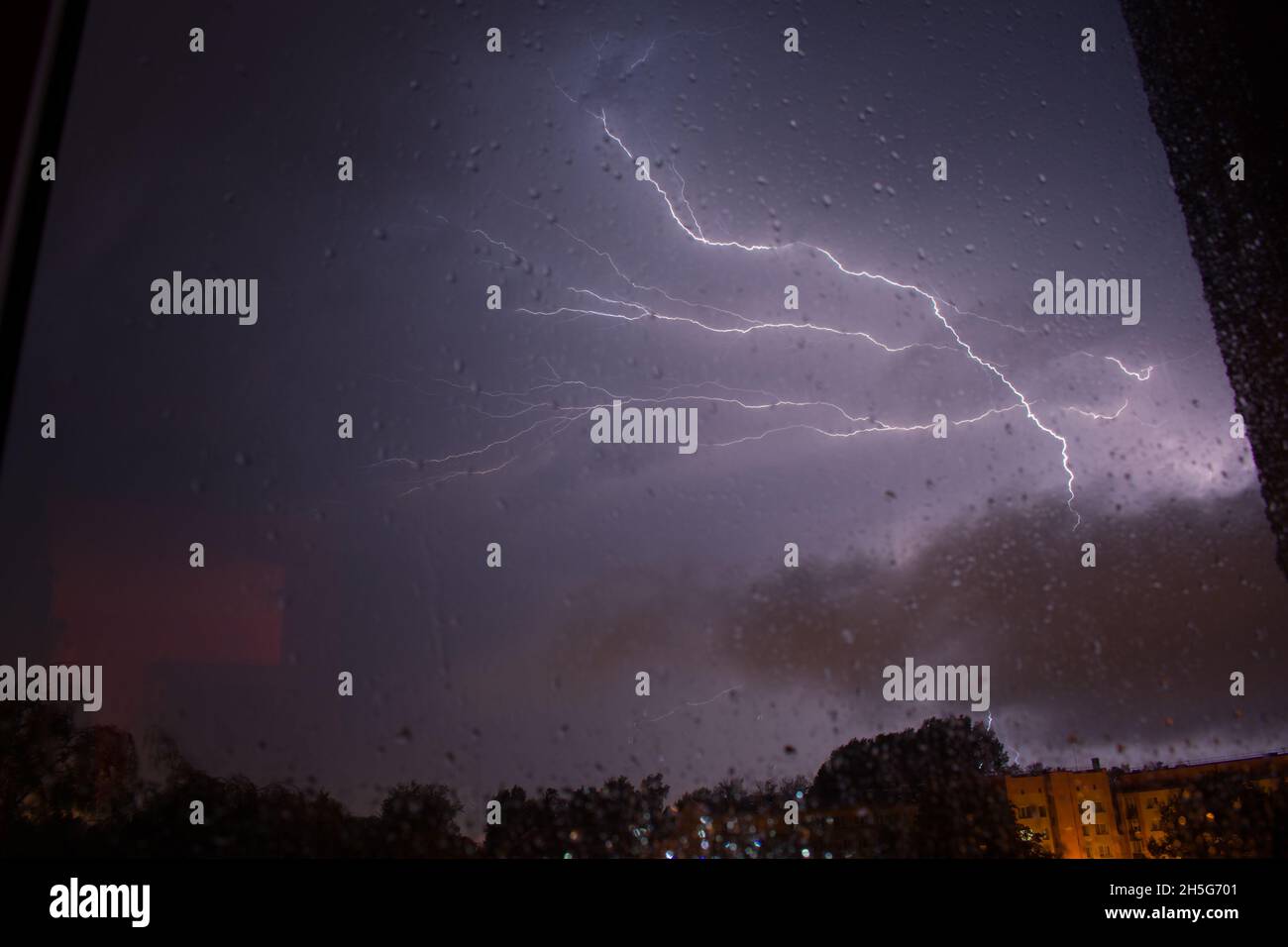 Lightning bolts striking in the dark cloudy night sky through a wet ...