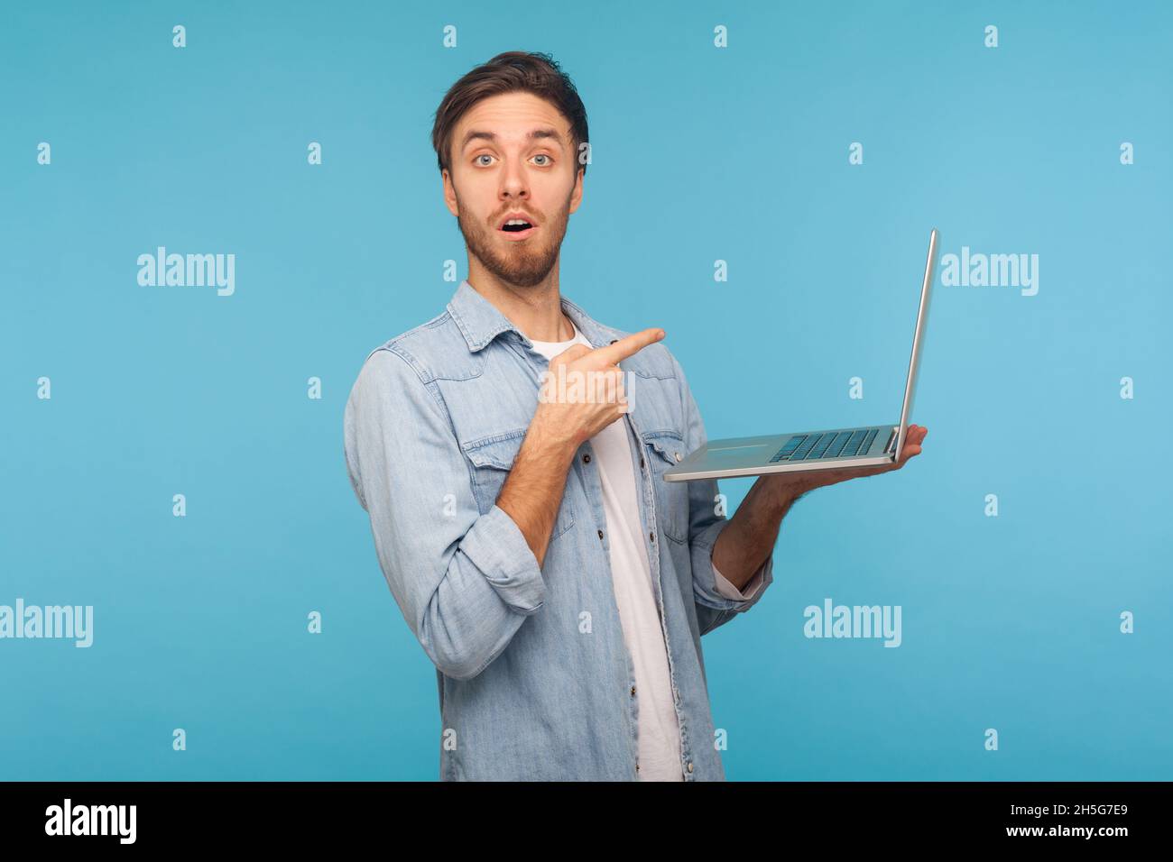 Portrait of shocked man wearing denim shirt, holding laptop and ...