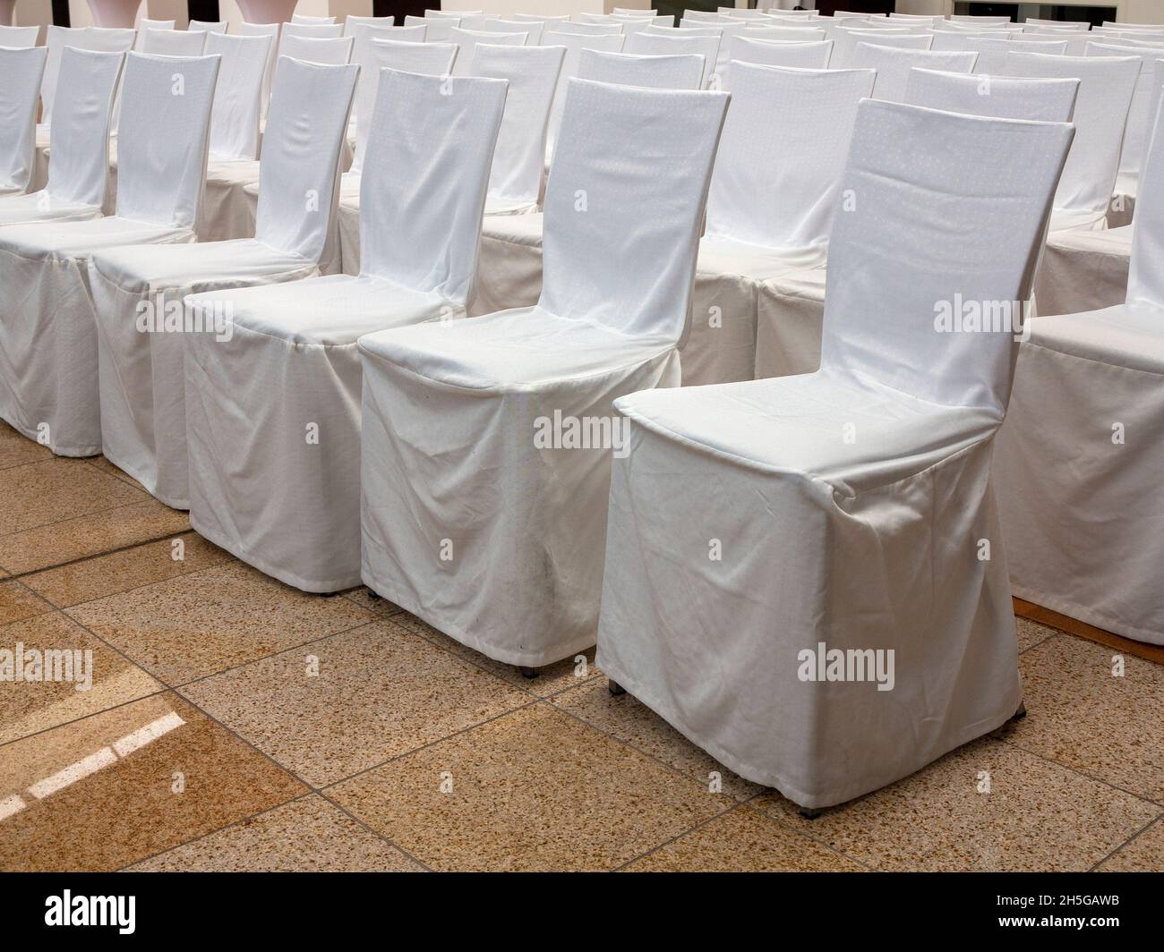 Many chairs in a row with white slipcovers Stock Photo - Alamy