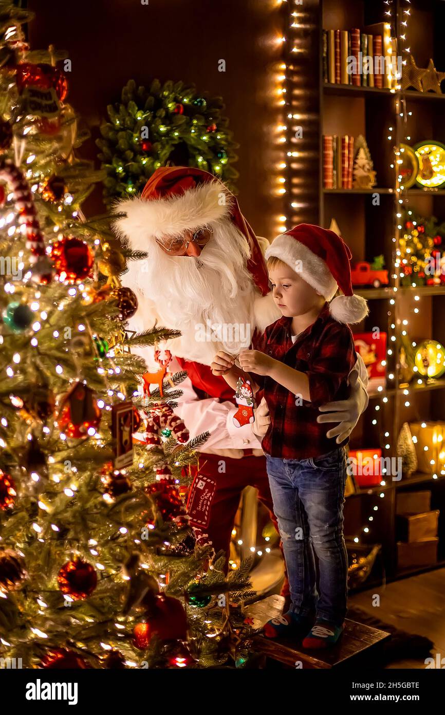 Santa Claus decorating Christmas tree with little boy assistant at home ...