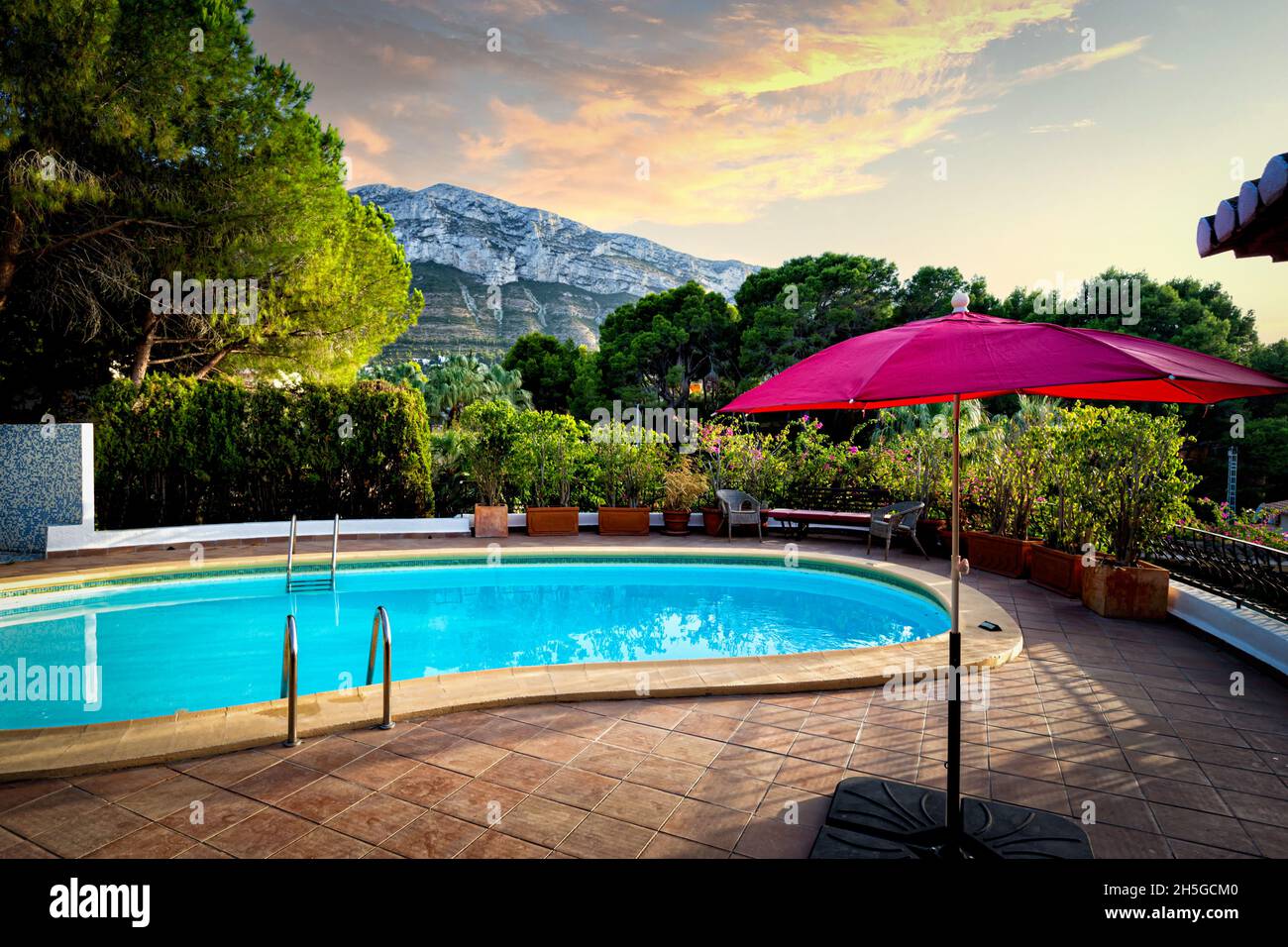 Blue pool under the pine trees with a red umbrella and a view of the ...