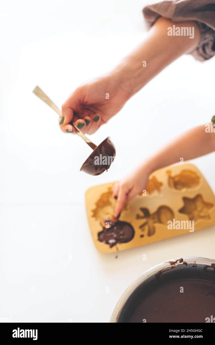 Children's and adults' hands pour a metal ladle of chocolate dough into ...